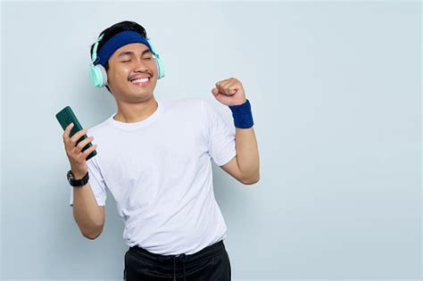 파란 머리띠와 흰색 티셔츠를 입은 젊은 아시아 남자 스포티 피트니스 트레이너 강사가 너무 기뻐했습니다 헤드폰으로 음악을 듣고