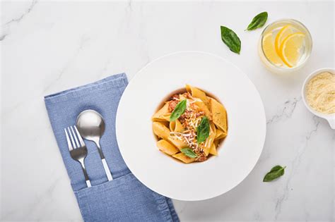 볼로네즈 페네 파스타 파마산 치즈 바질 볼로네즈 소스를 곁들인 맛있는 이탈리아 페네 파스타를 석판에 접시에 얹은 화이트 플레이트