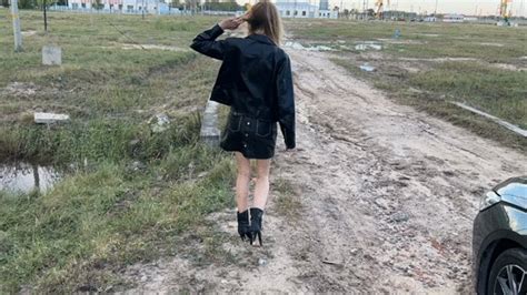 A Girl In Ankle High Boots In High Heels Walks Through A Ditch With Mud