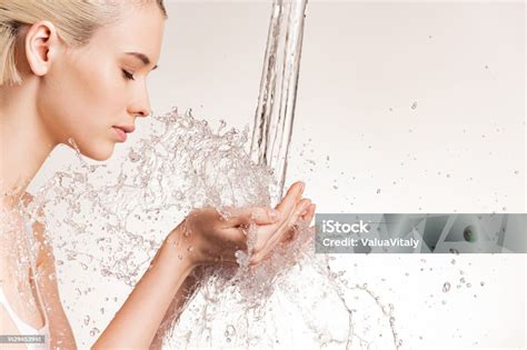 깨끗한 피부와 물 튀김을 가진 젊은 여성의 사진 금발의 여자 그녀의 얼굴 근처 물 방울 스파 트리트먼트 여자는 물로 손을 씻는다