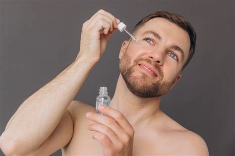 회색 스튜디오에서 뷰티 및 스킨케어 루틴 중에 뺨 근처에 세럼이 든 피펫을 들고 있는 잘생긴 미소 짓는 수염 난 남자 30 34세에 대한 스톡 사진 및 기타 이미지 Istock