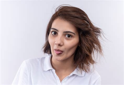 Drôle joyeuse jeune fille aux cheveux courts portant un polo blanc regardant la caméra qui sort