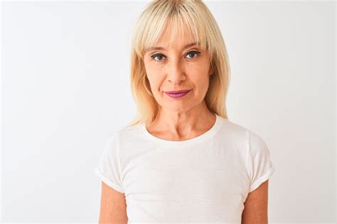 캐주얼 한 티셔츠를 입고 고립 된 흰색 배경 위에 서있는 중년 여성은 스마트 한 얼굴에 자신감있는 표정으로 심각한 생각을 하고