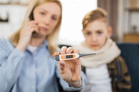 Mom Checking Temperature Of Her Sick Teen Son With High Fever Sitting On Sofa Stock Photo By