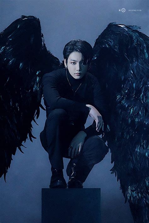 A Man Sitting On Top Of A Black Box Next To Two Large Black Angel Wings