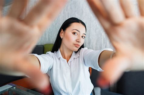 흰색 셔츠를 입은 예쁜 젊은 갈색 머리 아시아 여성을 클로즈업하고 자화상을 입고 손가락을 통해 찾고 손으로 삼각형 제스처를