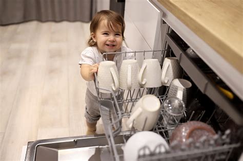 식기 세척기를 내리는 데 도움이되는 작은 귀여운 유아 소녀 집에서 흰색 부엌에서 재미있는 작은 엄마의 도우미 건강한 아이는 집안일을하고 있습니다 부엌에서 즐기는 아이 12