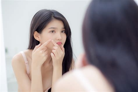 거울과 터치 얼굴을 찾고 아름 다운 젊은 아시아 여자는 여드름 Zit 치료 뷰티 걸 문제 아름다움과 가정에서 방에 얼굴에 주름진