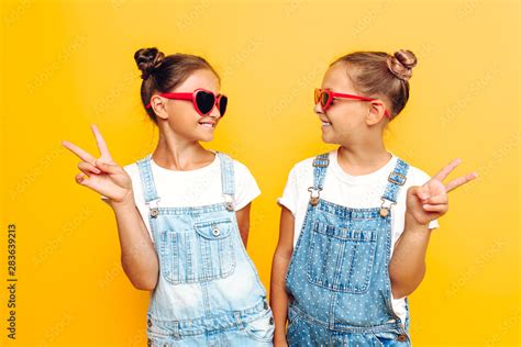 Two Teenage Girls Stylish Girlfriends In Sunglasses Posing On A Yellow