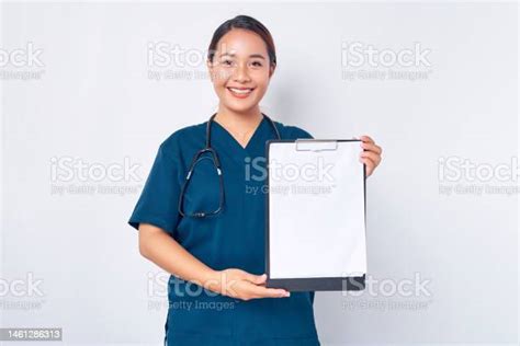 흰색 배경에 격리된 클립보드에 테스트 결과 또는 계약을 보여주는 청진기가 있는 파란색 유니폼을 입은 웃는 젊은 아시아 여성