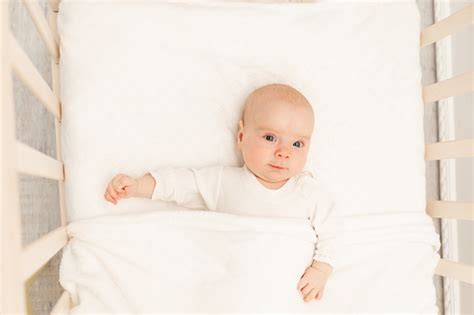 흰 침대에 아기의 초상화 어린이 방의 내부와 어린이를위한 침구 귀여운 어린 소녀가 침대에 누워 있다 아기는 흰색 침실에서 낮잠입니다 바디 파자마의 건강한 아이 명랑한에 대한