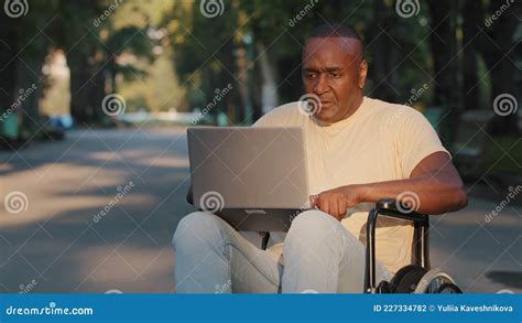 Adult Black Man On Wheelchair Uses Internet While Sitting Outdoors In