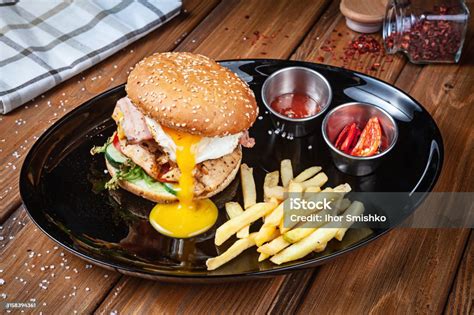 치킨 에그 양상추 소스를 곁들인 신선한 버거와 감자 튀김을 곁들인 블랙 플레이트 미국 패스트 푸드 나무 배경에 복사 공간이있는 치킨 버거 클로즈업 선택적 초점 음식 그릴