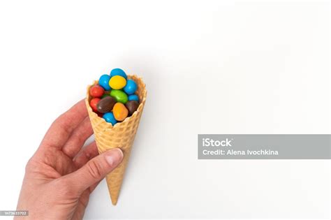 흩어져있는 여러 가지 빛깔의 둥근 사탕 당의정이있는 빈 와플 콘을 들고있는 손 즐거운 휴가 건강에 좋지 않은 음식에 대한 스톡