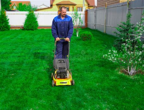 The Man Is Working In The Garden Mowing Grass With A Lawn Mower Stock