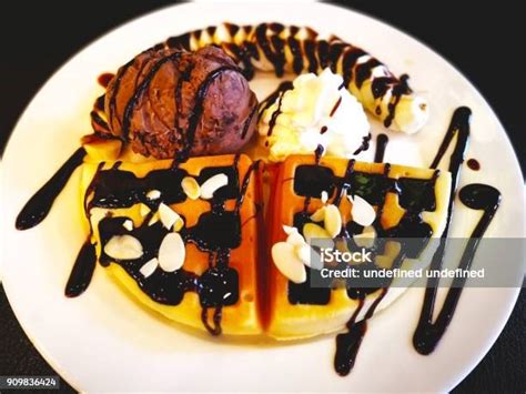 음식과 디저트 개념입니다 초콜릿 아이스크림 화이트 크림 와플 바나나를 슬라이스 하 고 액체 초콜릿 슬라이스 아몬드를 얹은 흰색 접시에 있다입니다 포그라운드에 초점 갈색에