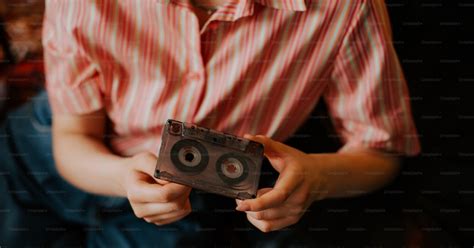 빨간색과 흰색 셔츠를 입은 남자가 검은색 물체를 들고 있다 사진 Unsplash의 카세트 테이프 이미지