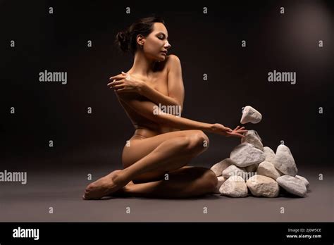 Naked Slim Woman Near Heap Of Levitating Stones In Studio Stock Photo