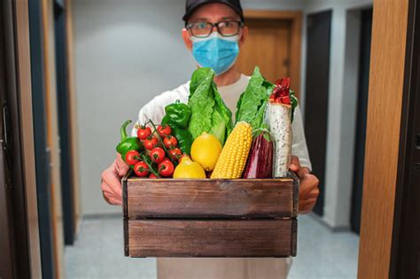 현관에 음식과 종이 봉투를 들고 보호 마스크에 배달 남자 택배는 고객에게 신선한 야채와 과일이있는 상자를 제공합니다 30 34