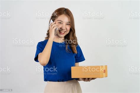 흰색 배경에 격리된 소포 상자를 들고 행복하게 웃고 있는 스마트폰을 들고 있는 아시아 여성 온라인 특급 배송 및 쇼핑 비즈니스