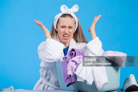 아침에 다림질을 위해 접힌 세탁 그릇에있는 깨끗한 옷의 양에 놀란 여자 소녀는 스튜디오의 파란색 배경에 서있는 겁에 질린 분노를