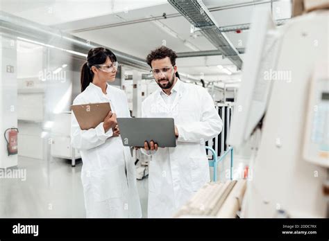 Female Scientist Looking At Male Colleague Using Laptop In Laboratory