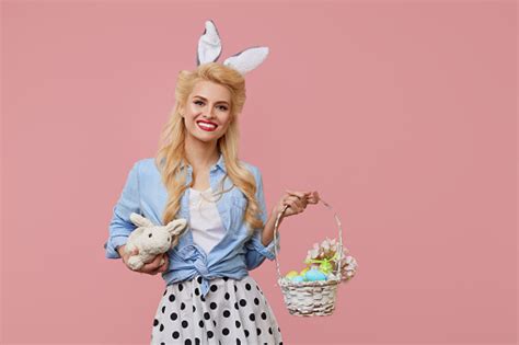 행복한 부활절 토끼 귀를 가진 젊은 핀 업 여자는 분홍색 배경에 유기농 색깔의 계란으로 가득 찬 바구니를 들고 있습니다 행복한 얼굴 0에 대한 스톡 사진 및 기타 이미지