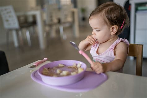 한 아이 작은 백인 유아 여성 아기는 방에서 집에서 혼자 테이블에서 먹는 숟가락을 잡고 실제 사람들이 공간을 복사 초기 아동