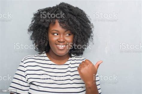 젊은 아프리카계 미국인 플러스 크기 여자 생기고 엄지 측면 가리키는 행복 한 얼굴로 웃 고 회색 그런 지 벽에 T 셔츠에 대한