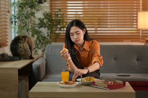 Beautiful Asian Girl Eating Pizza With Pleasure Sitting On Couch In