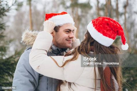 산타 모자를 쓰고 겨울 철엽 숲에서 포옹하고 장난을 치며 커플 20 29세에 대한 스톡 사진 및 기타 이미지 20 29세
