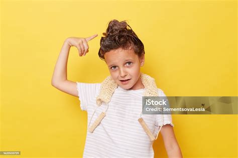 하얀 티셔츠를 입고 어깨에 수건을 두른 채 노란 배경 위에 고립되어 서 있는 젖은 머리에 샴푸를 손가락으로 가리키는 재미있는