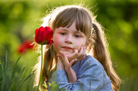 회색 눈과 밝은 빨간 튤립 꽃과 긴 머리와 귀여운 예쁜 미소 아이 소녀 흐린 햇볕이 잘 드는 녹색 보케 배경에 자연 개념에 사랑 감정에 대한 스톡 사진 및 기타 이미지