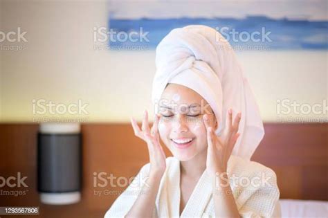 침실 스킨 케어 및 트리트먼트 컨셉의 얼굴에 보습 크림을 바르는 화이트 목욕 가운의 행복한 아름다운 여성 건강관리와 의술에 대한