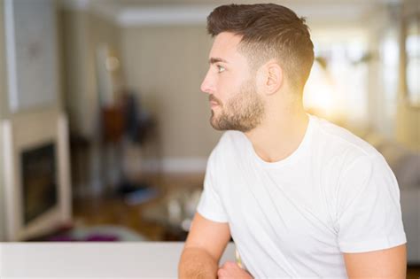 젊은 잘생긴 남자 캐주얼 흰색 T 셔츠를 입고 집에서 측면을 찾고 자신감 미소와 함께 자연 스러운 얼굴로 프로필 포즈를 휴식 T 셔츠에 대한 스톡 사진 및 기타 이미지