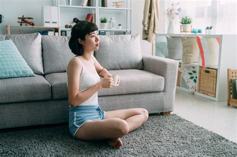 모닝 커피 일상 생활 방식 개념을 즐기십시오 큰 창문 옆에서 커피를 마시는 짧은 머리를 가진 젊은 아시아 한국 여성의 초상화 햇빛이있는 집 거실에 앉아있는 귀여운 소녀