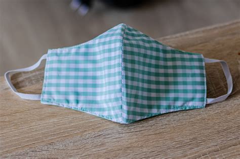 나무 테이블에 녹색으로 배치 격자 무늬 천으로 만든 수제 얼굴 마스크 세척 및 재사용 코로나 바이러스 전염병으로 인해 수술 마스크의 부족 중에 사용할 수 있습니다 바이러스