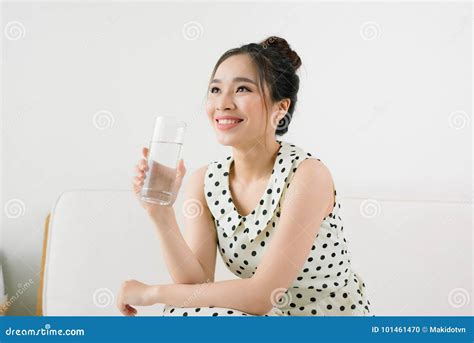 Young Beautiful Asian Woman Holding A Glass Of Water While Sitting At