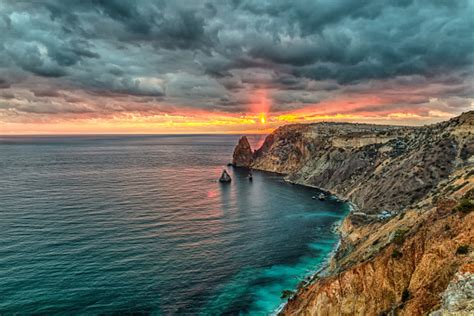 일몰 동안 해변의 바다 풍경 바위 절벽은 따뜻한 일몰에 의해 조명된다 긴 노출 흐릿한 구름 공간을 복사합니다 평온한 침묵과 자연과의 단합의 개념 0명에 대한 스톡 사진 및