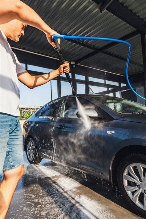 A Man Washes His Car At A Self Service Car Wash Using A Hose With