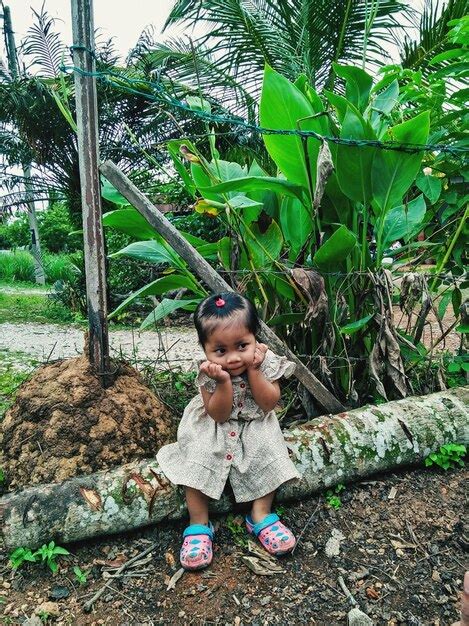 Premium Photo Cute Girl Sitting On Log Against Plants At Park