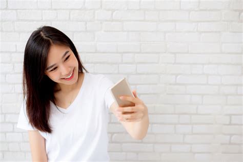 아름 다운 초상화 젊은 아시아 여자 콘크리트 시멘트 흰색 배경에 스마트 휴대 전화 Selfie를 복용 소녀 행복으로 촬영과 재미