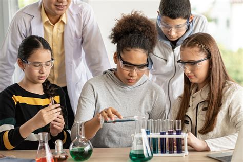 実験室で化学実験を行う理科の授業で保護眼鏡をかけた学生の多様性グループ試験管で化学を混ぜる女の子を見ている先生学習と教育のコンセプト