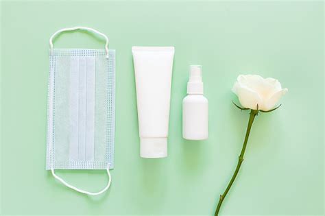 파란색 외과 용 보호 마스크 액체 항균 스프레이 스퀴즈 병 플라스틱 튜브 및 밝은 녹색 배경에 흰색 장미의 상단 보기 브랜딩 및 라벨을 위한 브랜드가 없는 화이트 병 모형