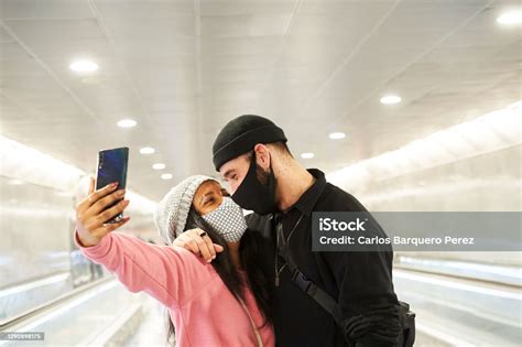 지하철이나 공항 복도에서 셀카를 찍는 얼굴 마스크와 양모 모자를 쓴 젊은 인종 간 커플 공항에 대한 스톡 사진 및 기타 이미지
