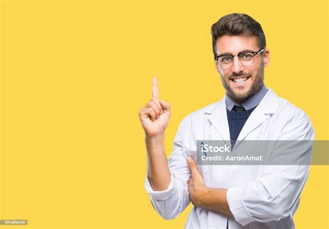 잘생긴 젊은이 입고 의사 Scientis 카메라 보고 측면을 손과 손가락으로 가리키는 얼굴에 큰 미소와 함께 고립 된 배경 위에