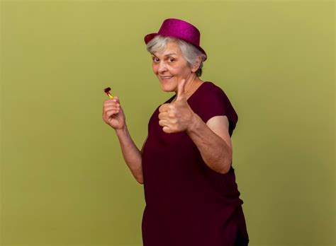 Free Photo Smiling Elderly Woman Wearing Party Hat Thumbs Up And Holds Whistle Isolated On