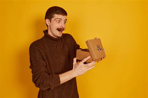 노란색 스튜디오 배경에 고립 된 놀라움으로 선물 상자를 여는 젊은 감정적인 남자의 초상화 행복한 감정 25 29세에 대한 스톡