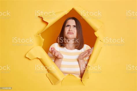 줄무늬 티셔츠를 입고 노란 종이 찢어진 구멍을 뚫고 서서 울고 올려다 보며 이유를 말하고 슬픔과 슬픔을 표현하는 슬픈 화가 난