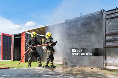 뜨거운 불타는 화재와 컨테이너에서 위험한 연기 비상 사고 구조에 대한 물 화재 호스를 사용하여 제복을 가진 소방관 또는 소방관의 그룹 사람 영웅 팀워크 소방관에 대한 스톡